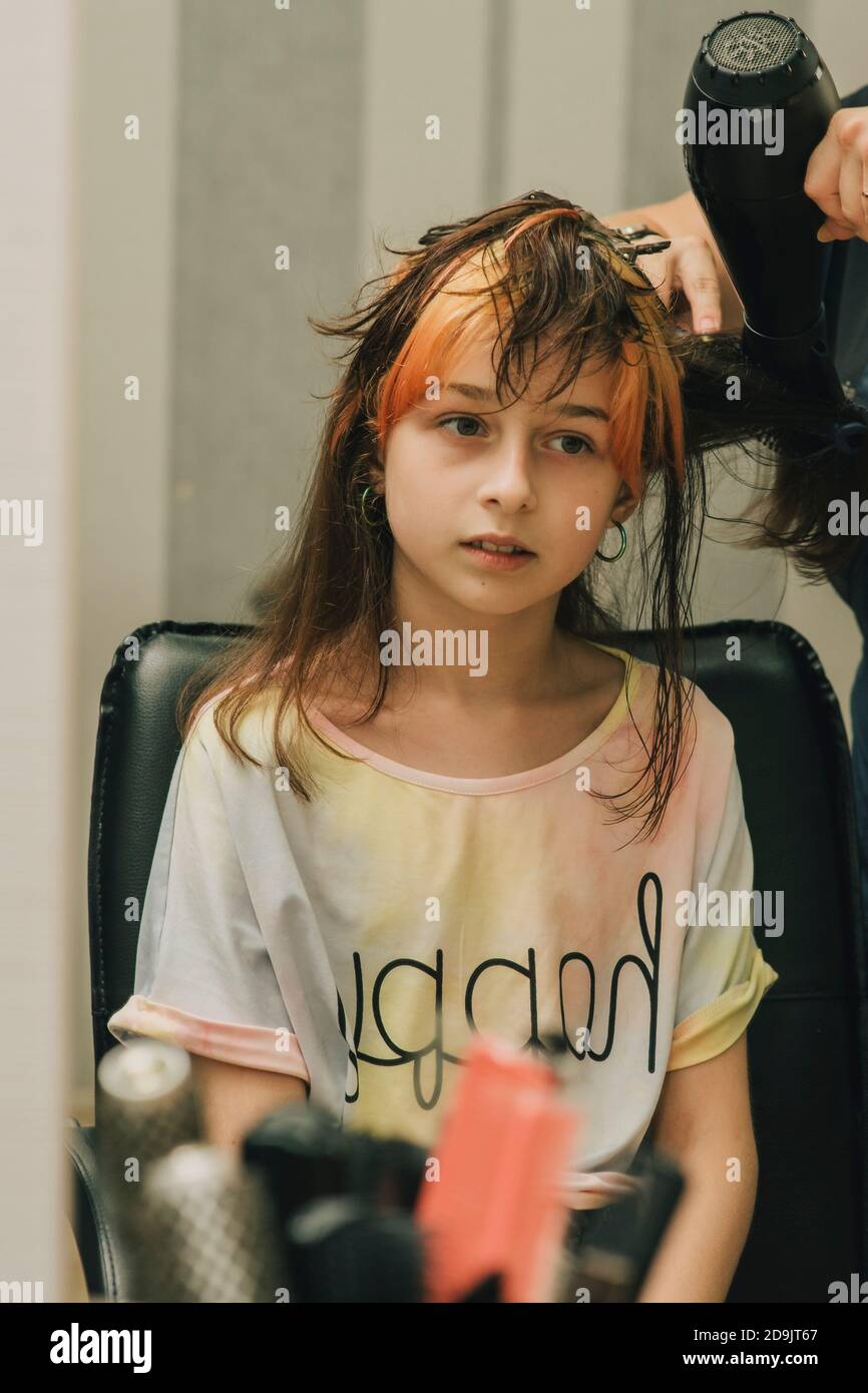 Hairdresser making a hair style to cute little girl. A teenage girl has ...