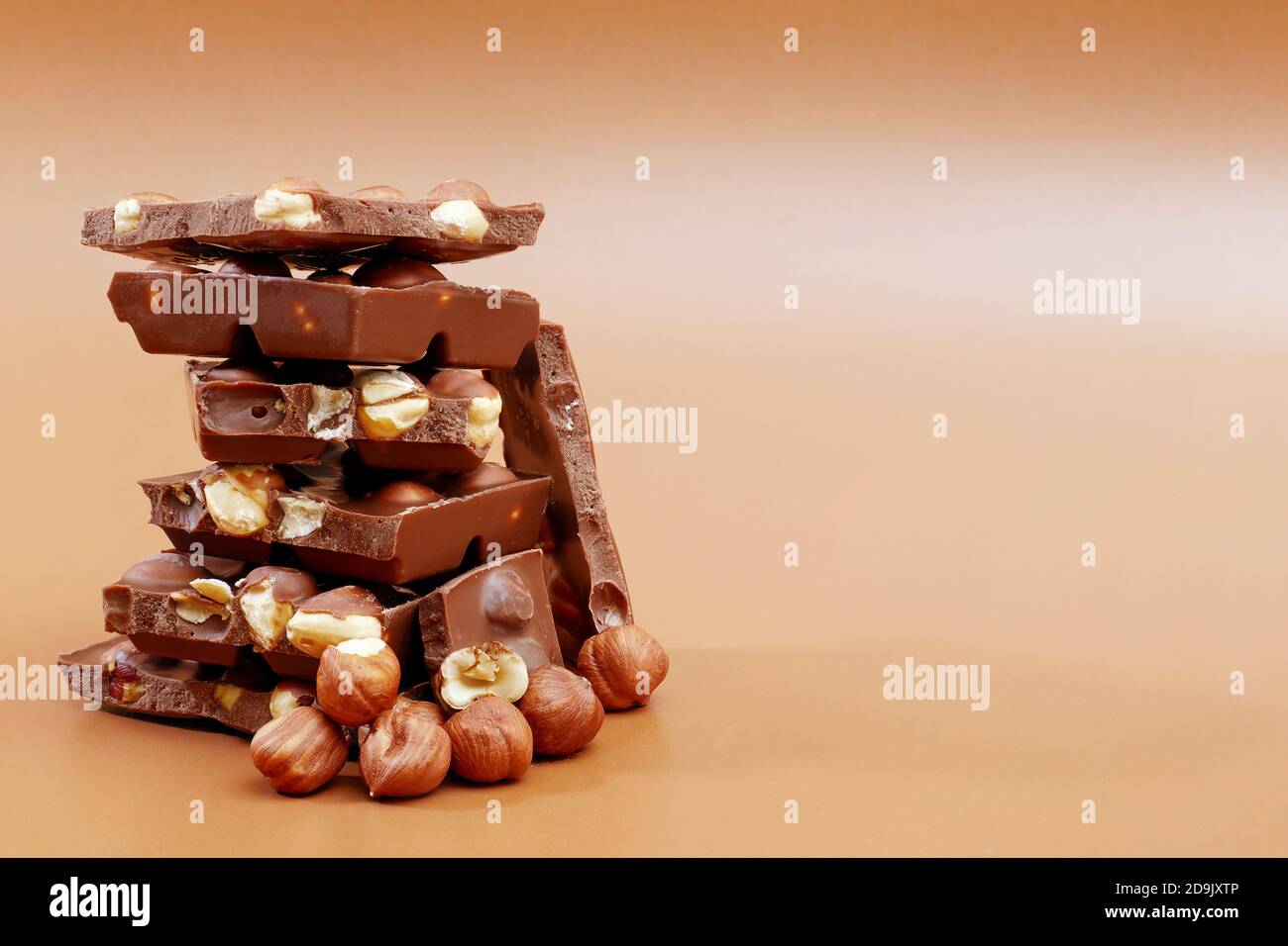stack of milk chocolate pieces and hazelnuts on brown background with ...