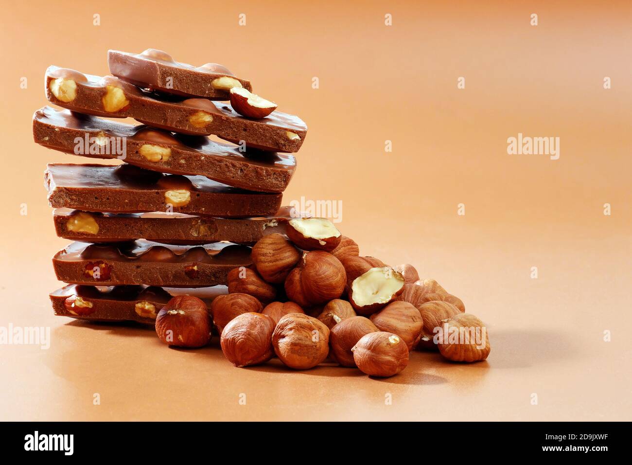 stack of milk chocolate pieces and hazelnuts on brown background with ...