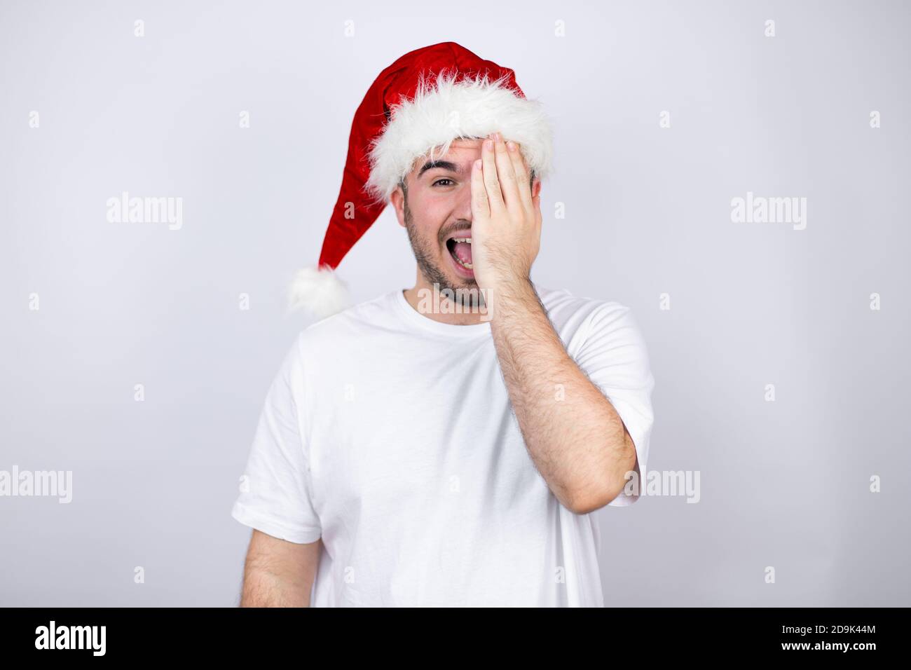 Young handsome man wearing a Santa hat over white background covering ...
