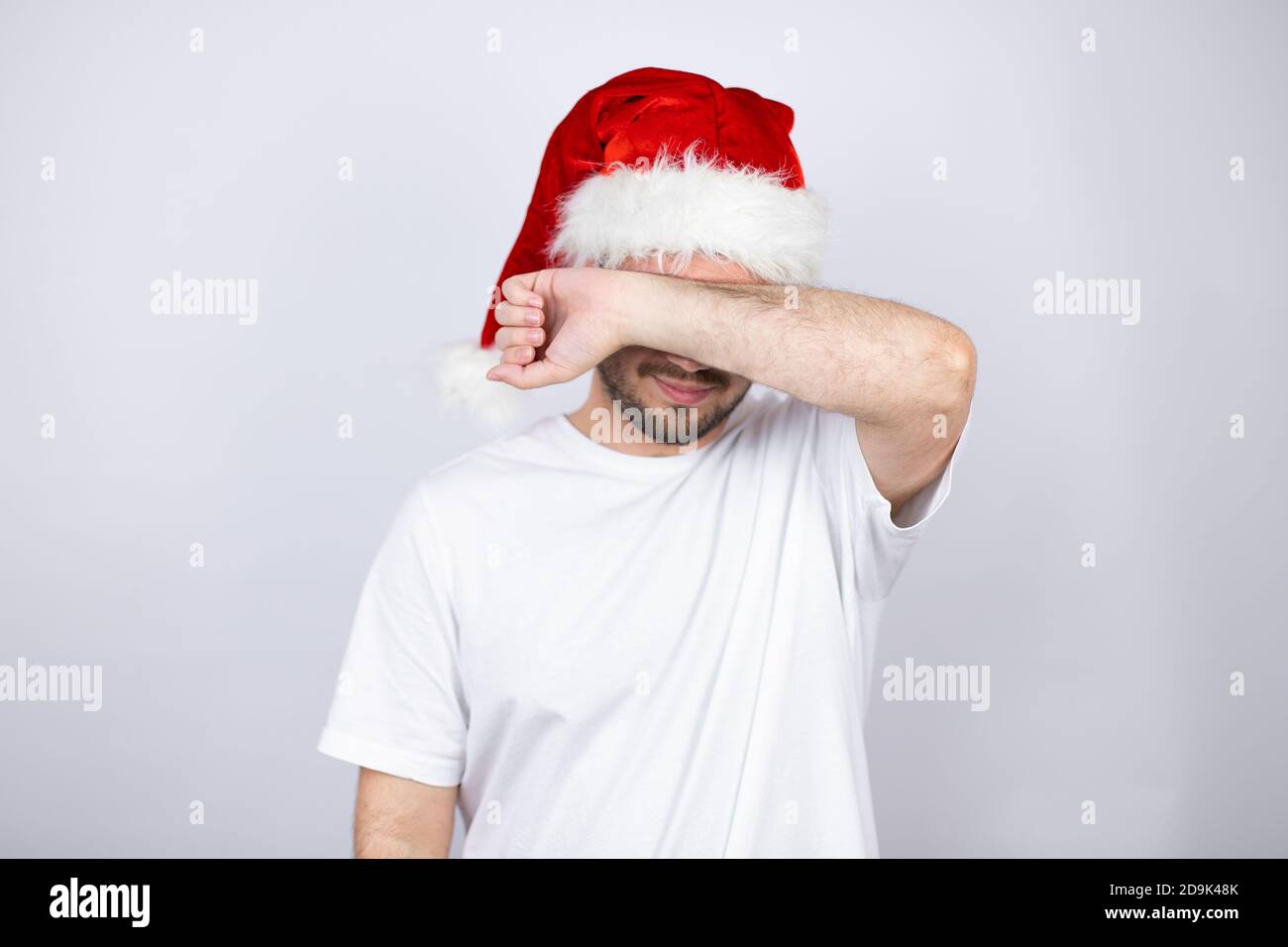 Young handsome man wearing a Santa hat over white background covering ...