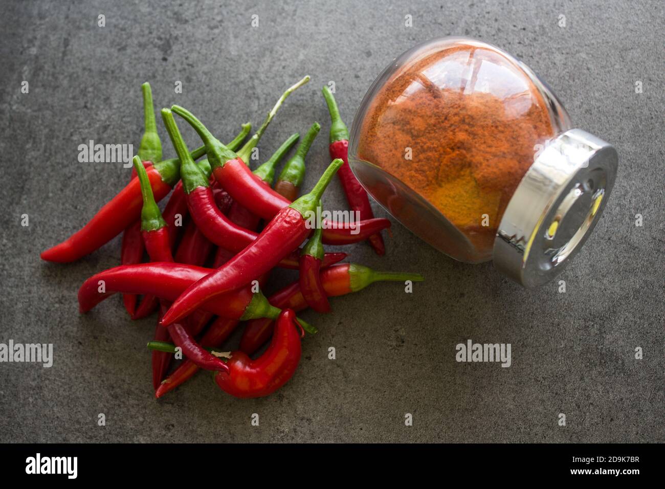 Red chili peppers and paprika powder in glass spice jar on stone table ...