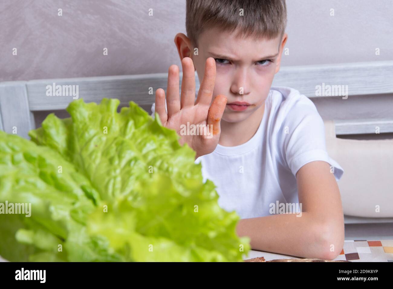 A Caucasian boy refuses to eat salad, with an open hand makes a stop ...