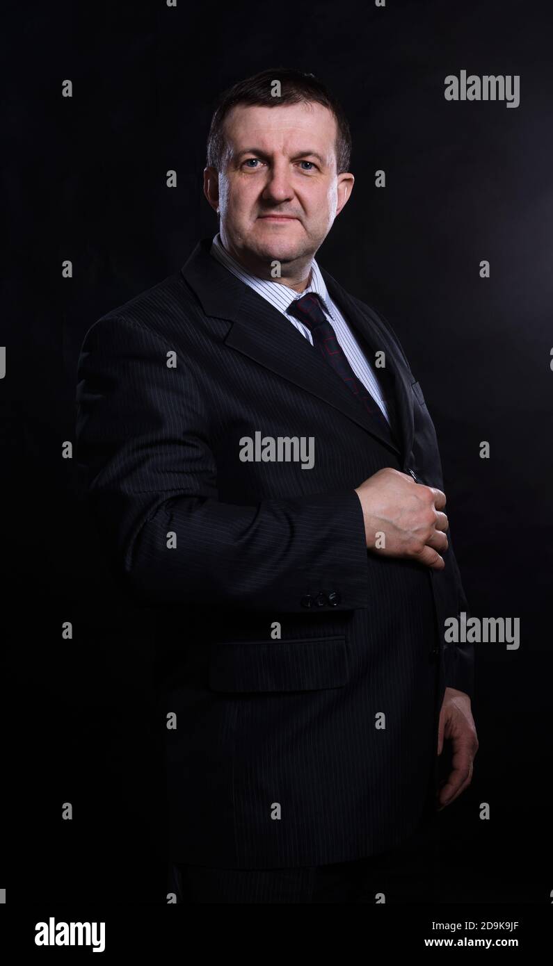 Middle aged solid man dressed in suit studio portrait on black ...