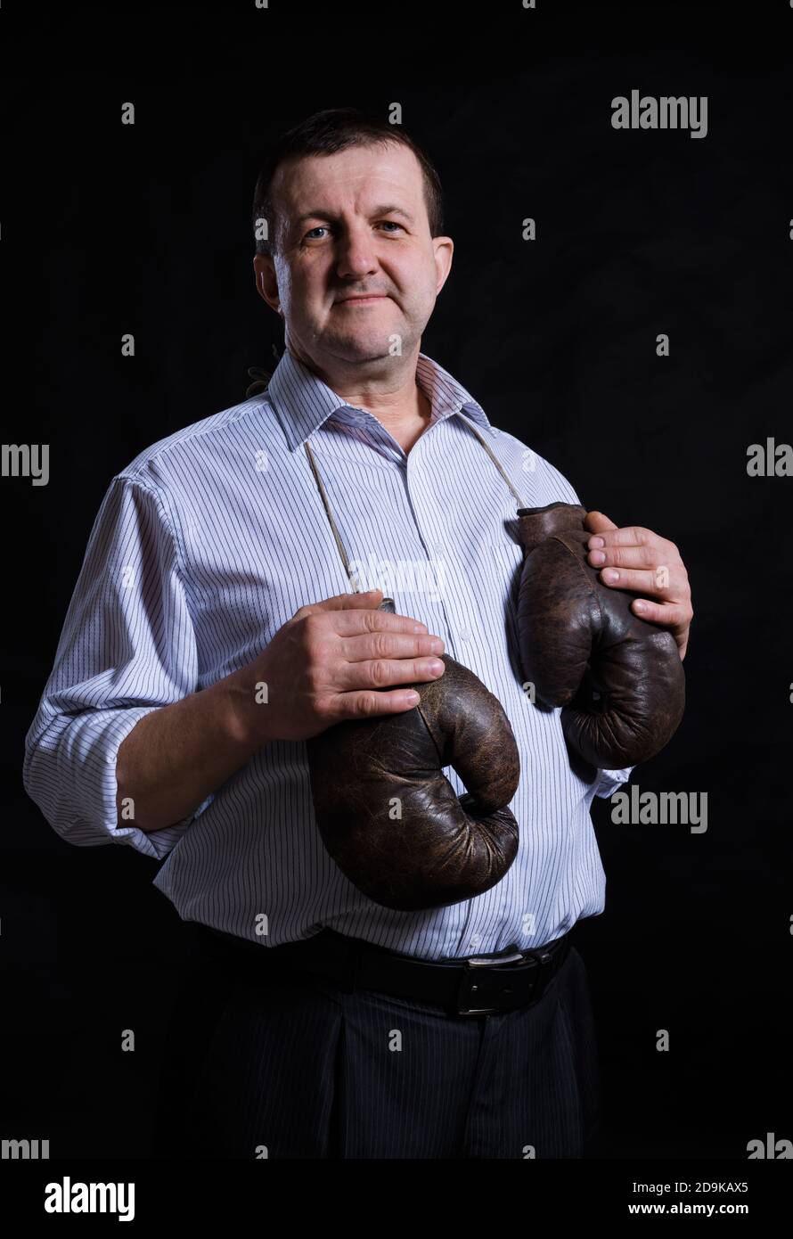 Middle aged solid man with old boxing gloves dressed in shirt studio ...