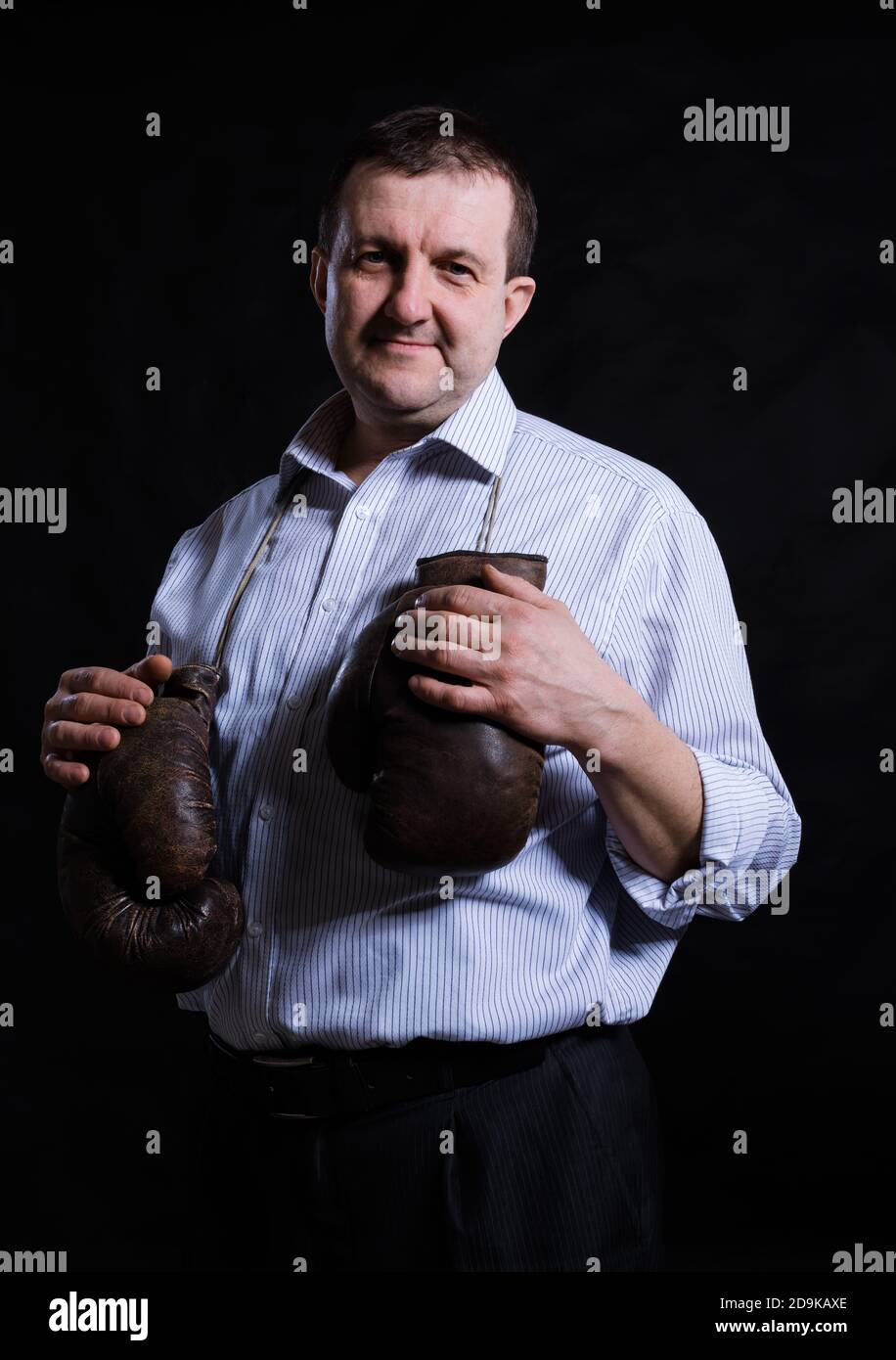Middle aged solid man with old boxing gloves dressed in shirt studio ...