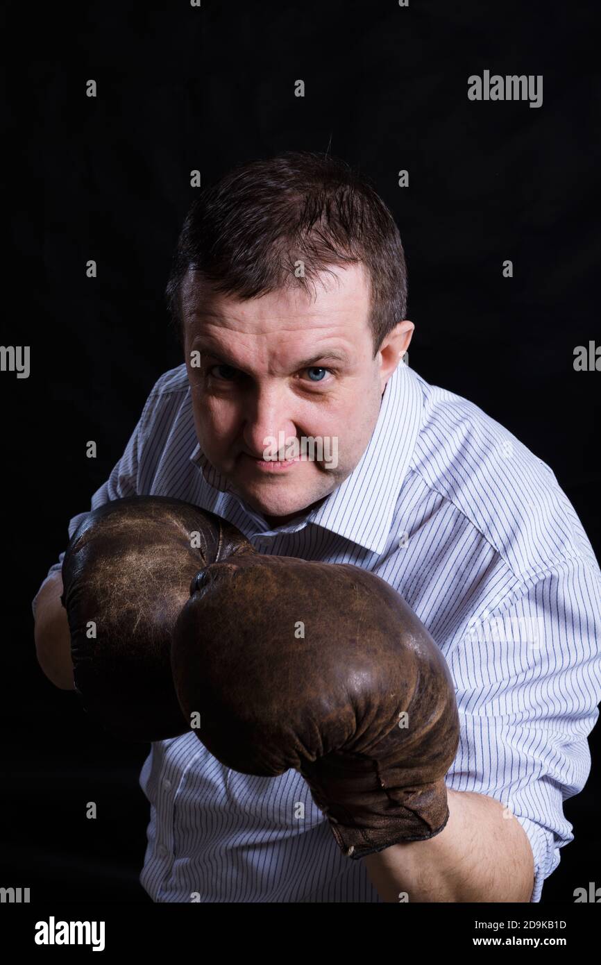 Middle aged solid man with old boxing gloves dressed in shirt studio ...