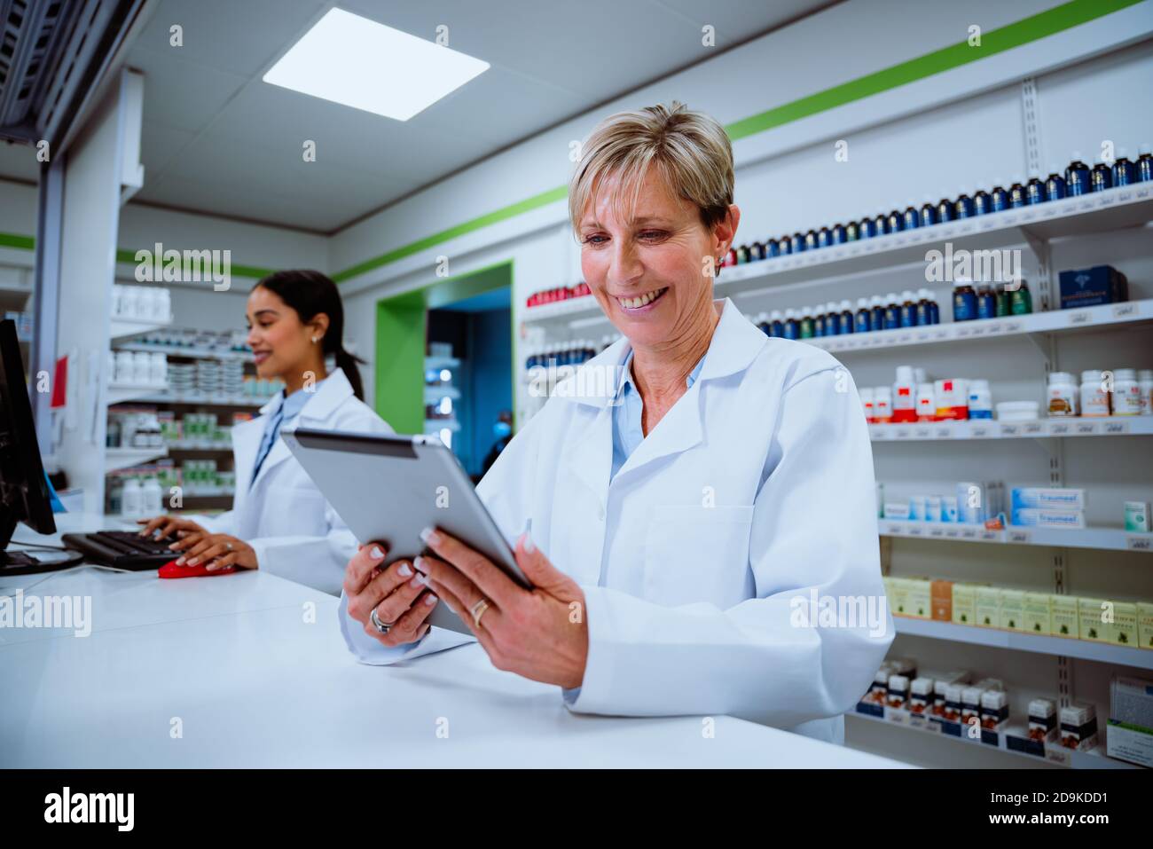 Senior pharmacist scrolling through digital tablet standing behind ...