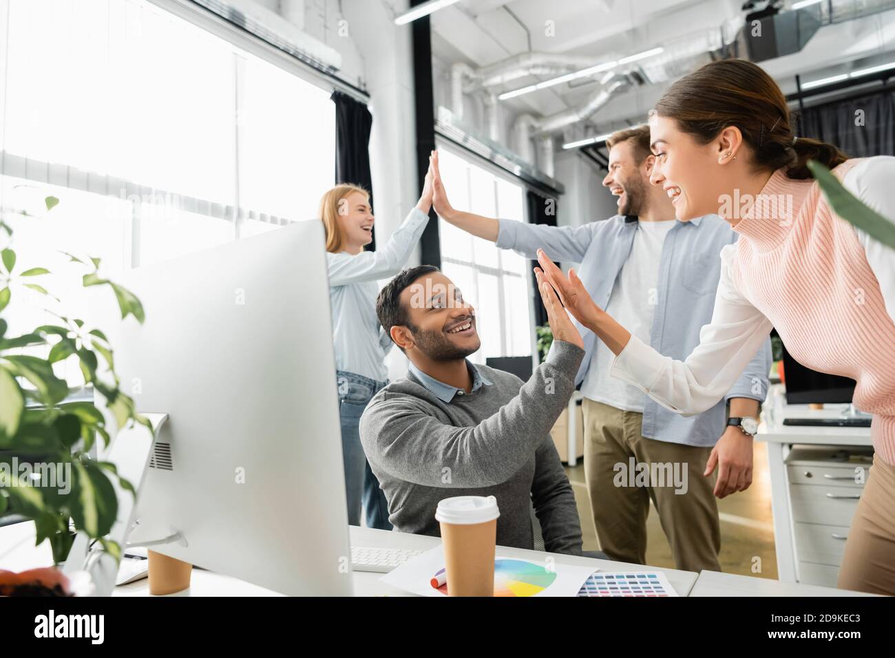 Cheerful multicultural businesspeople giving high five near computer ...