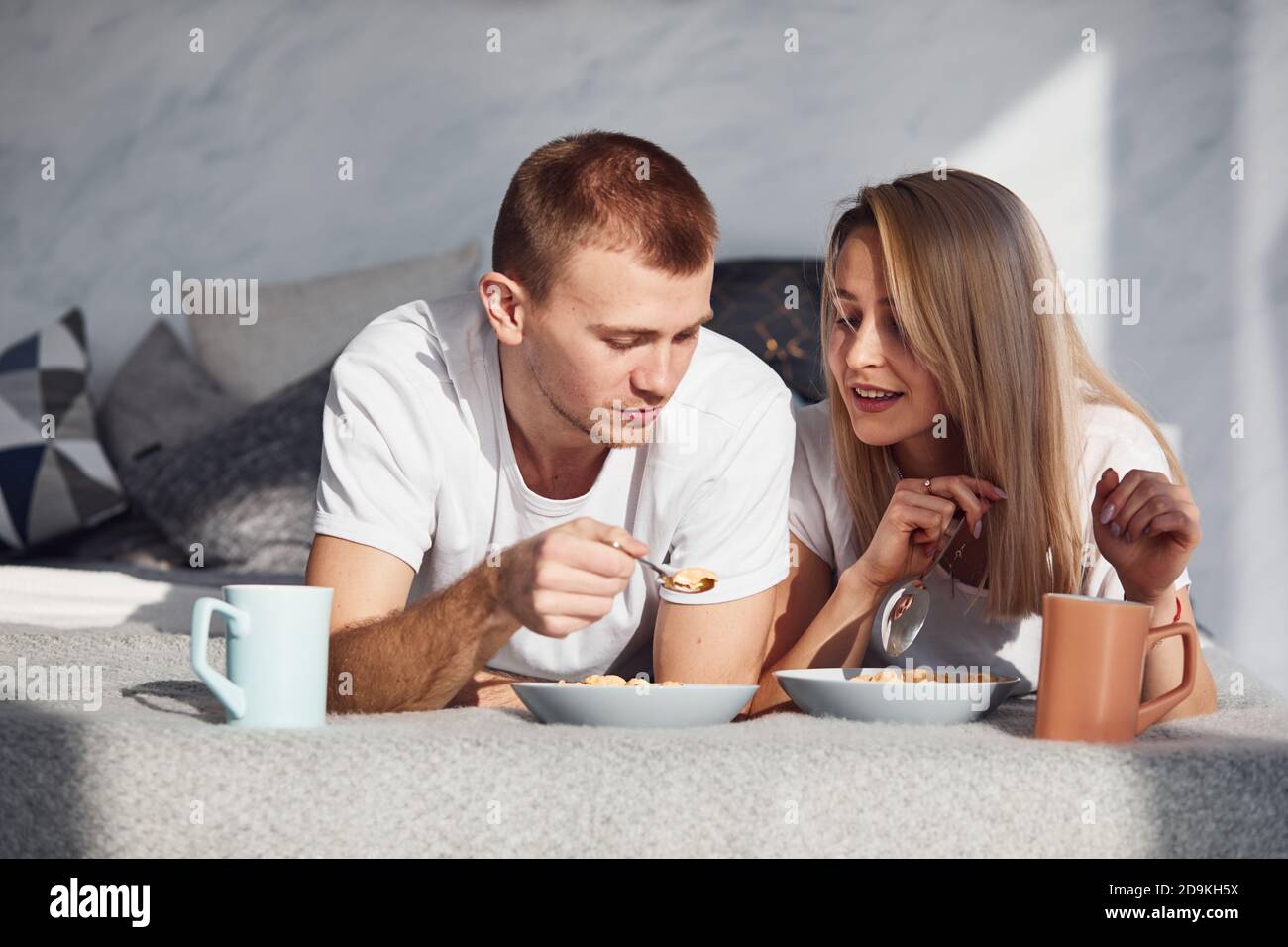 Young lovely couple have a breakfast at home while lying down on bed ...