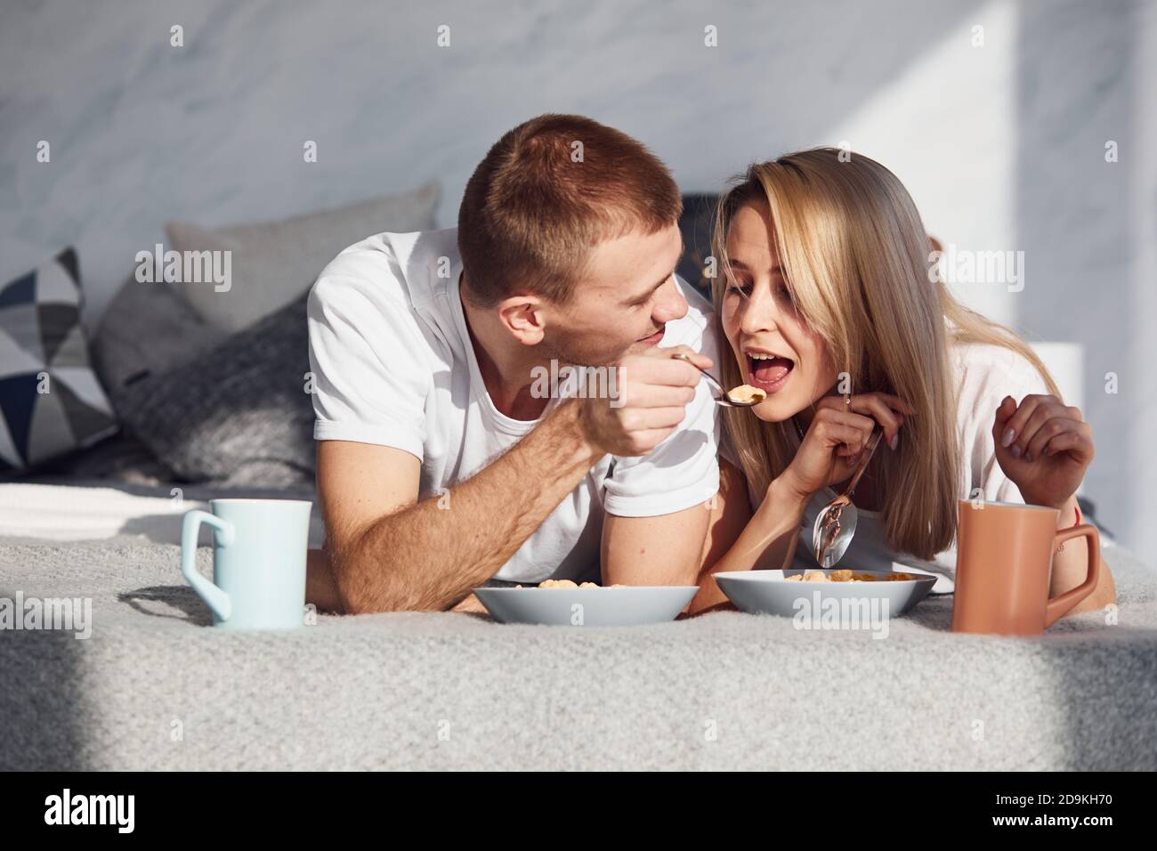 Young lovely couple have a breakfast at home while lying down on bed ...
