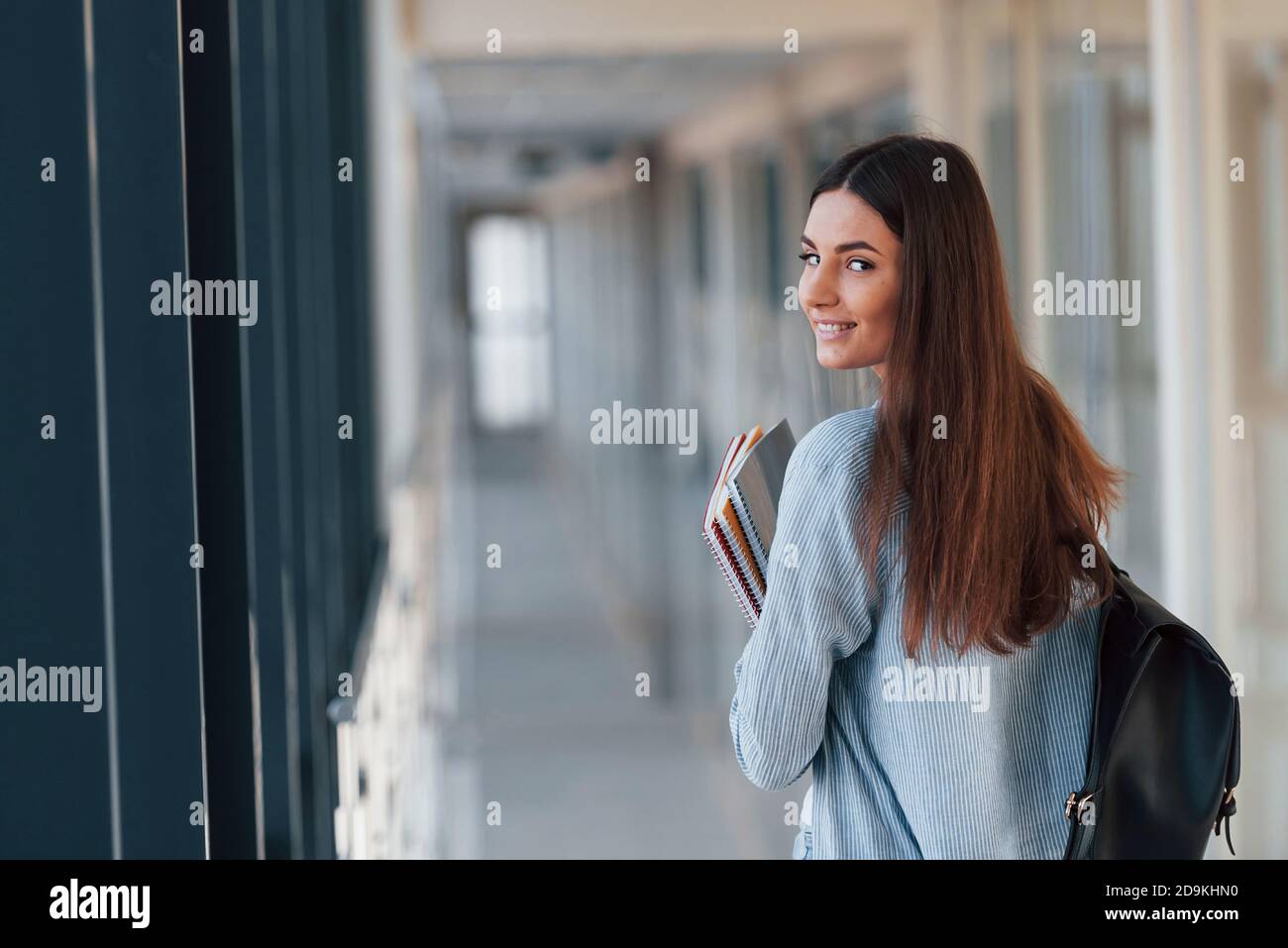 Rear view of female young student that is in corridor of a college and ...