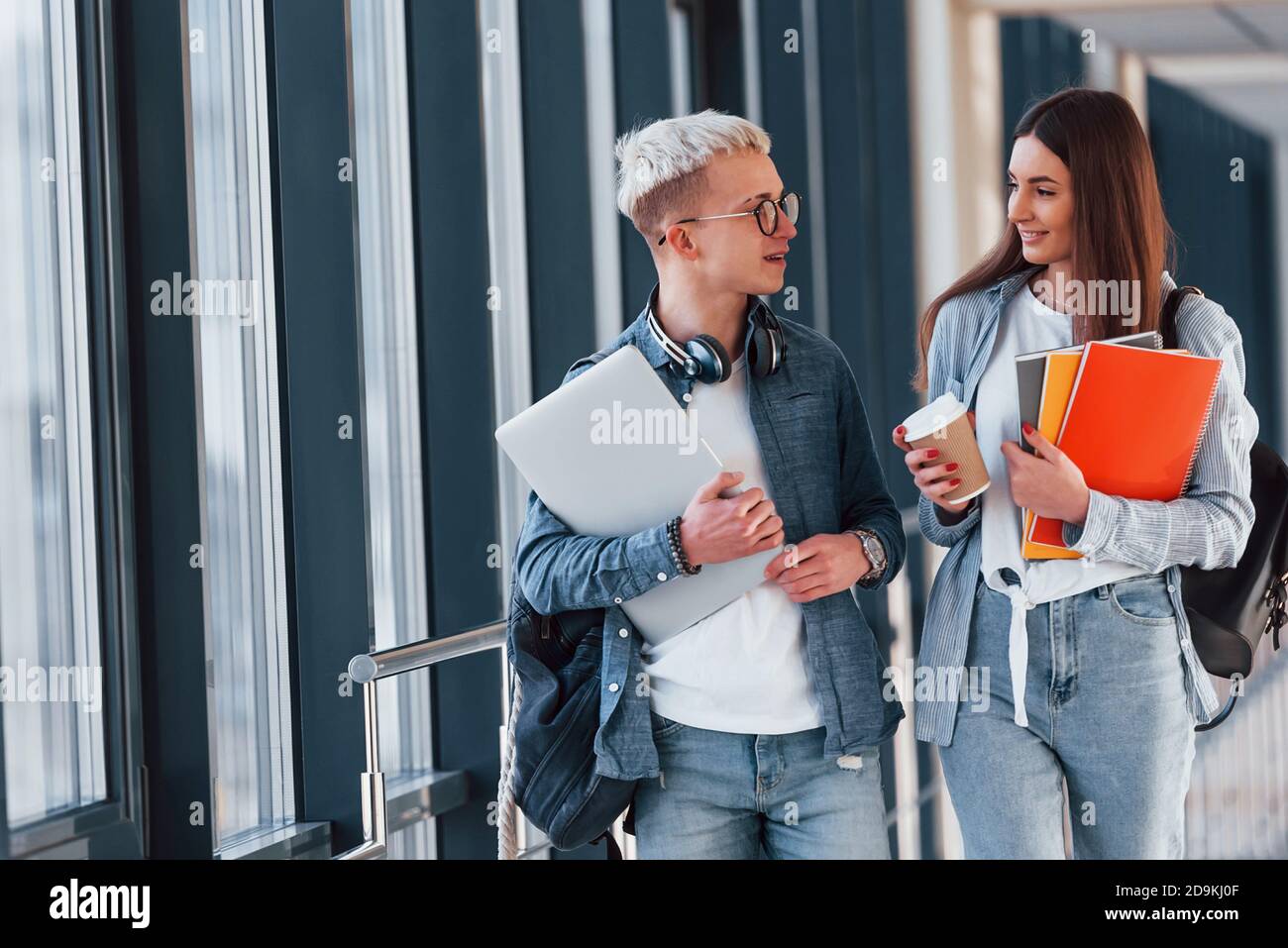 Two young student friends together in a corridor of a college walking ...