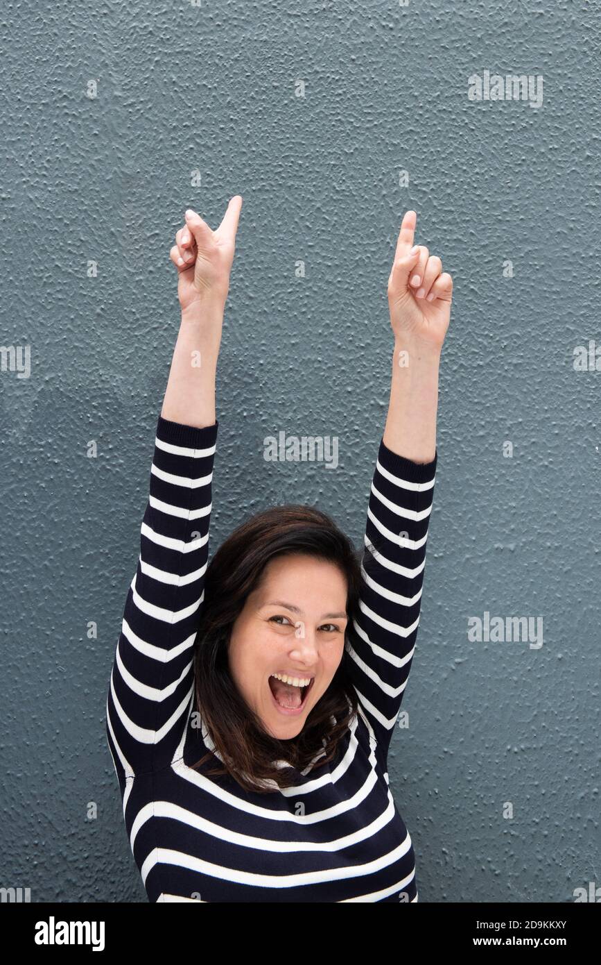 Portrait cheerful young woman with arms raised and fingers pointing up ...