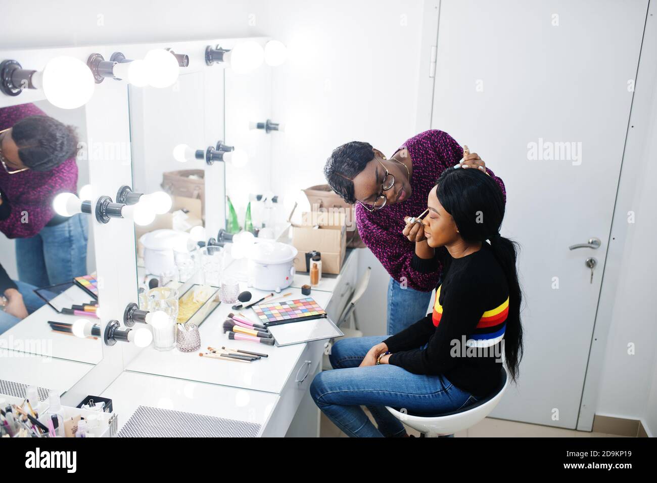 African American woman applying make-up by make-up artist at beauty ...