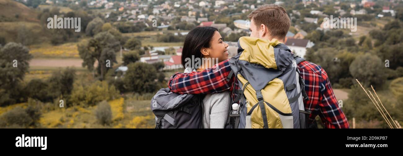 Back view of man with backpack hugging african american girlfriend ...