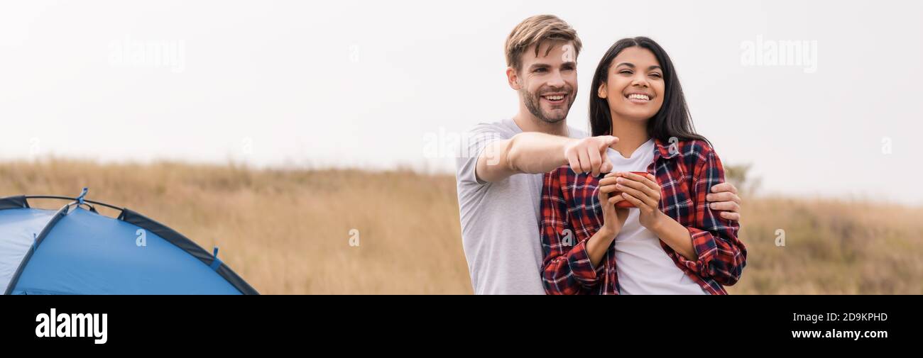 Man pointing with finger near smiling african american woman with cup ...