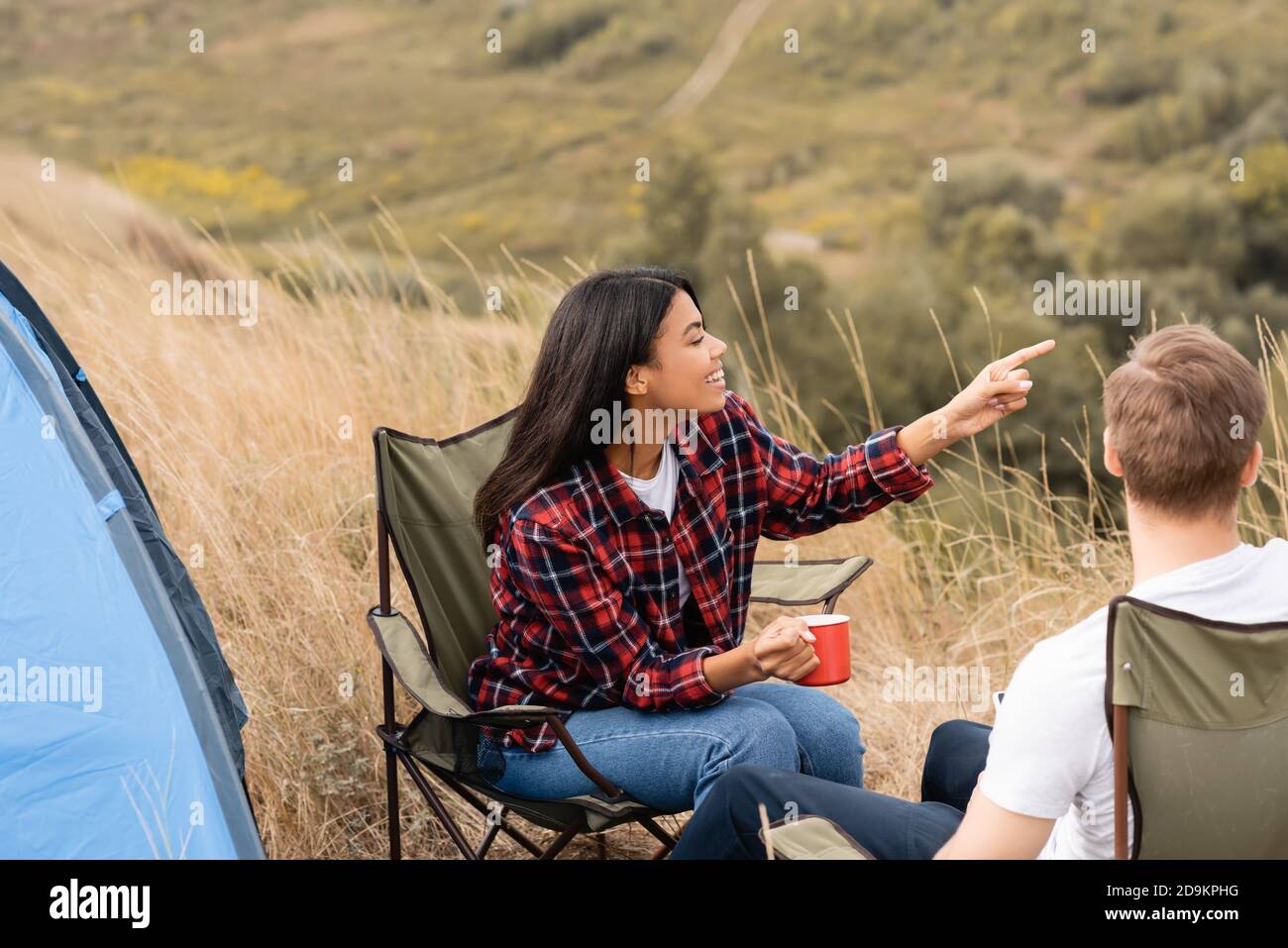 Smiling african american woman with cup pointing with finger while ...
