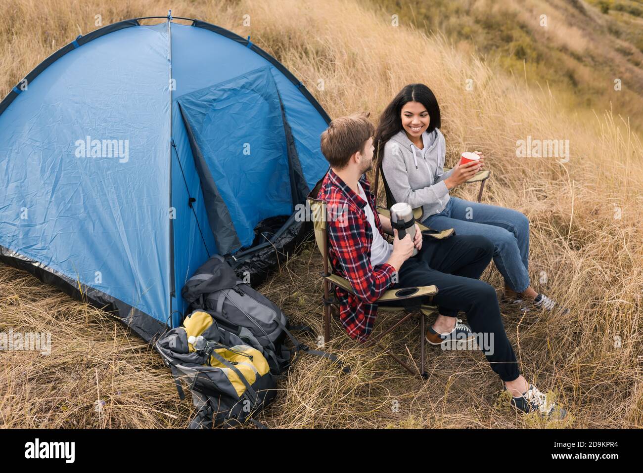 African american woman holding cup near boyfriend with thermos and tent ...