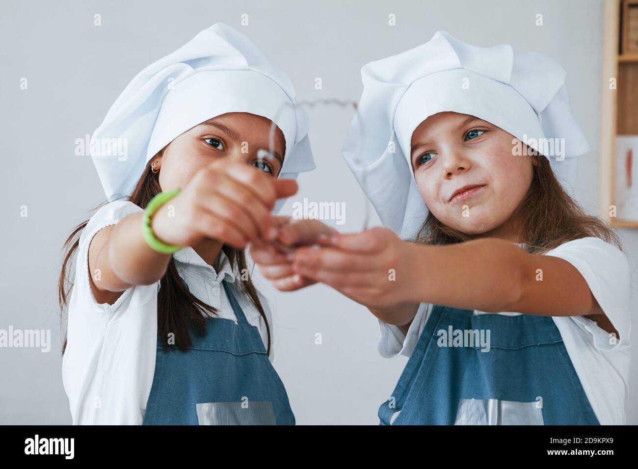 Two little girls in blue chef uniform working with flour on the kitchen ...