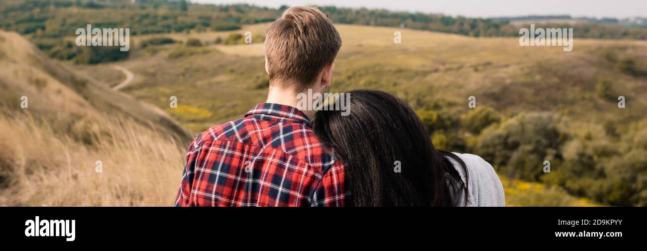 Back view of young travelers standing with grassy landscape on blurred ...