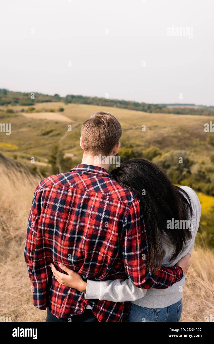 Back view of multiethnic couple hugging with hills on blurred ...