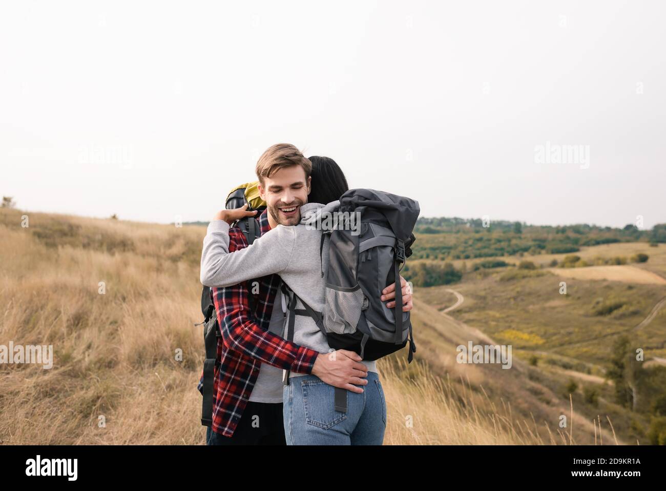 Smiling traveler with backpack embracing african american woman during ...