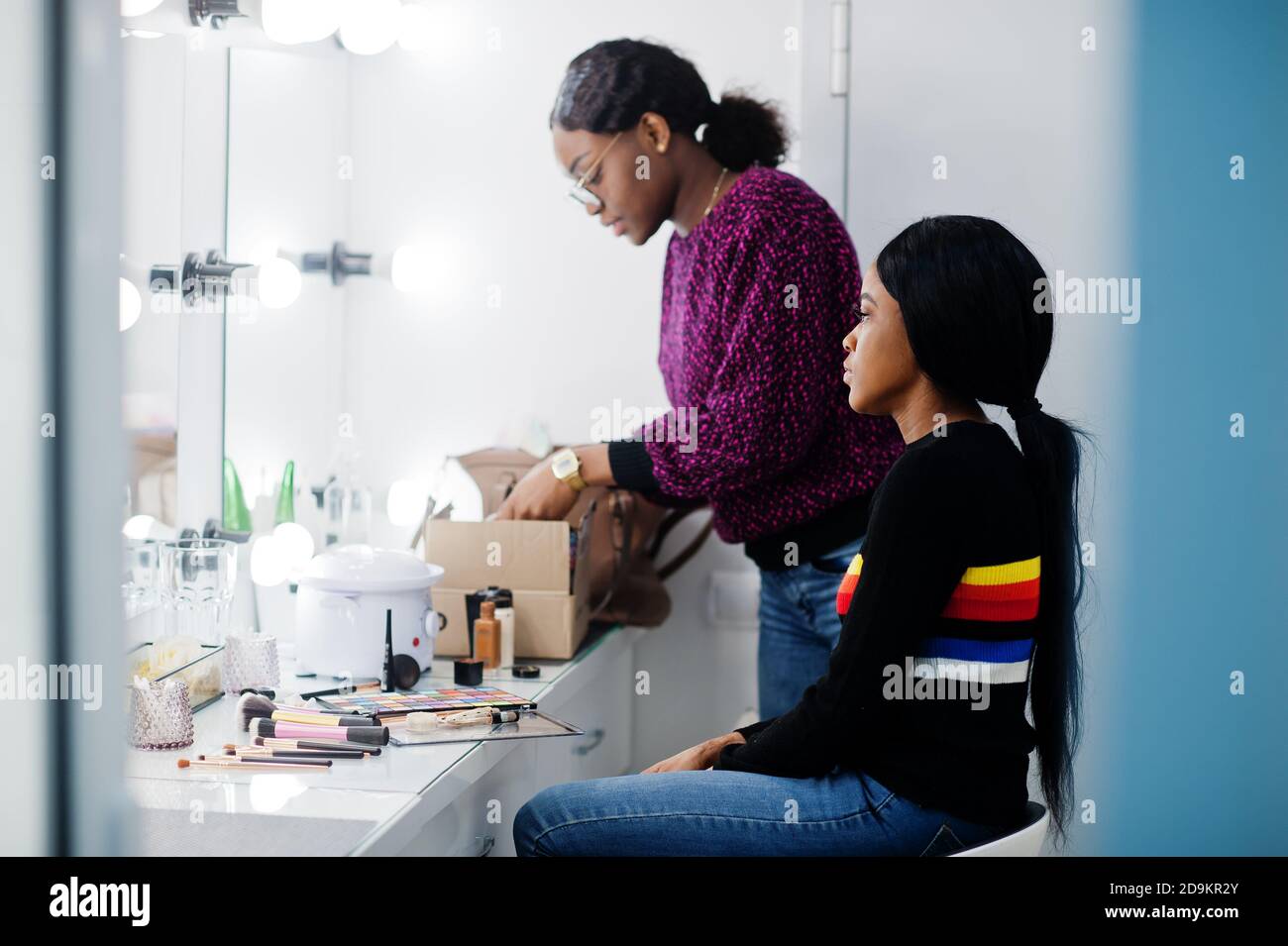 African American woman applying make-up by make-up artist at beauty ...