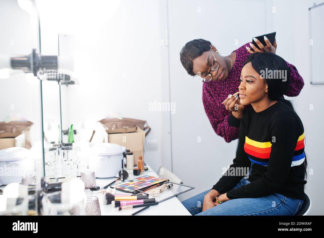 African American woman applying make-up by make-up artist at beauty ...