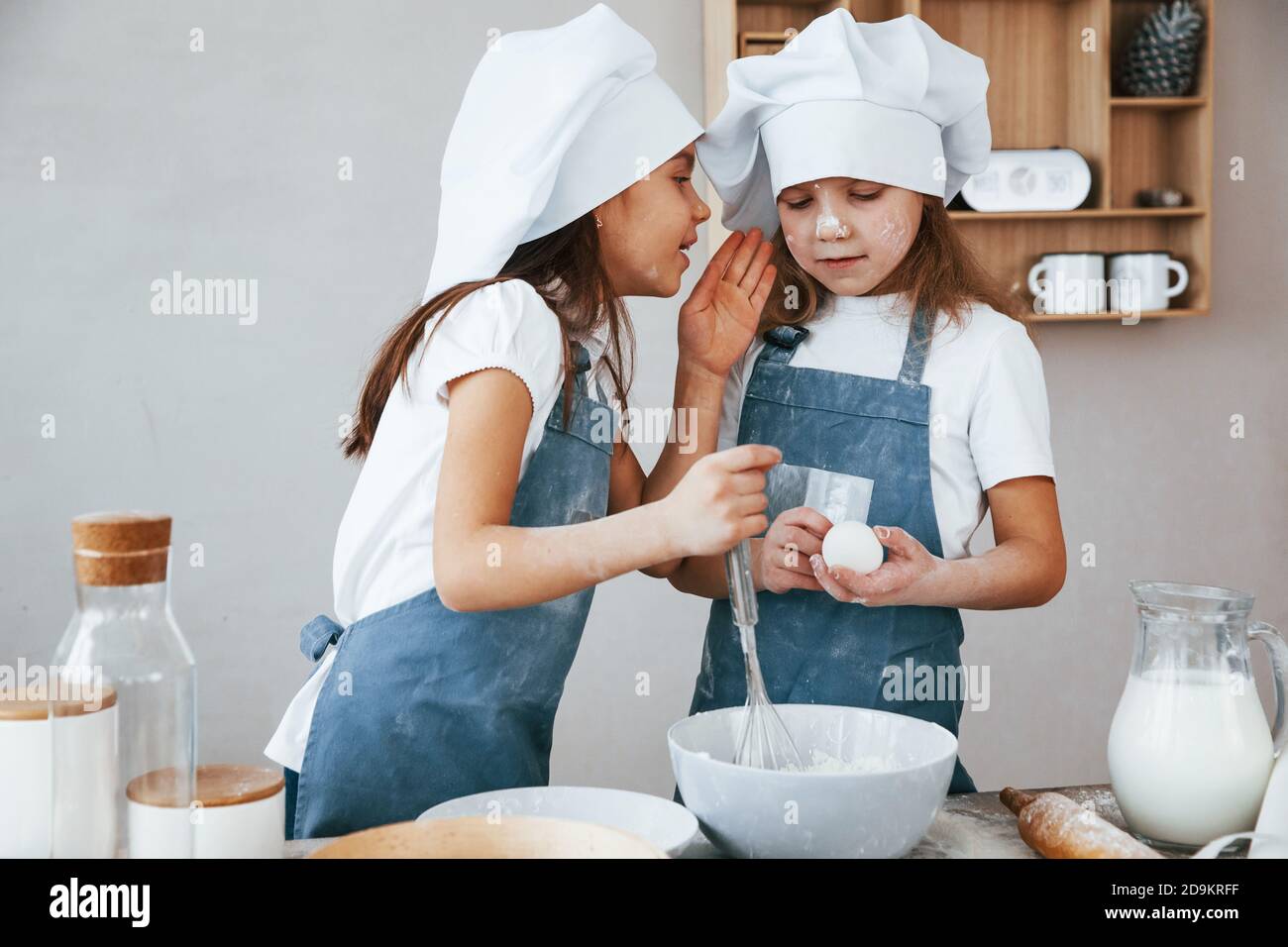 Two little girls in blue chef uniform talking secrets to each other ...