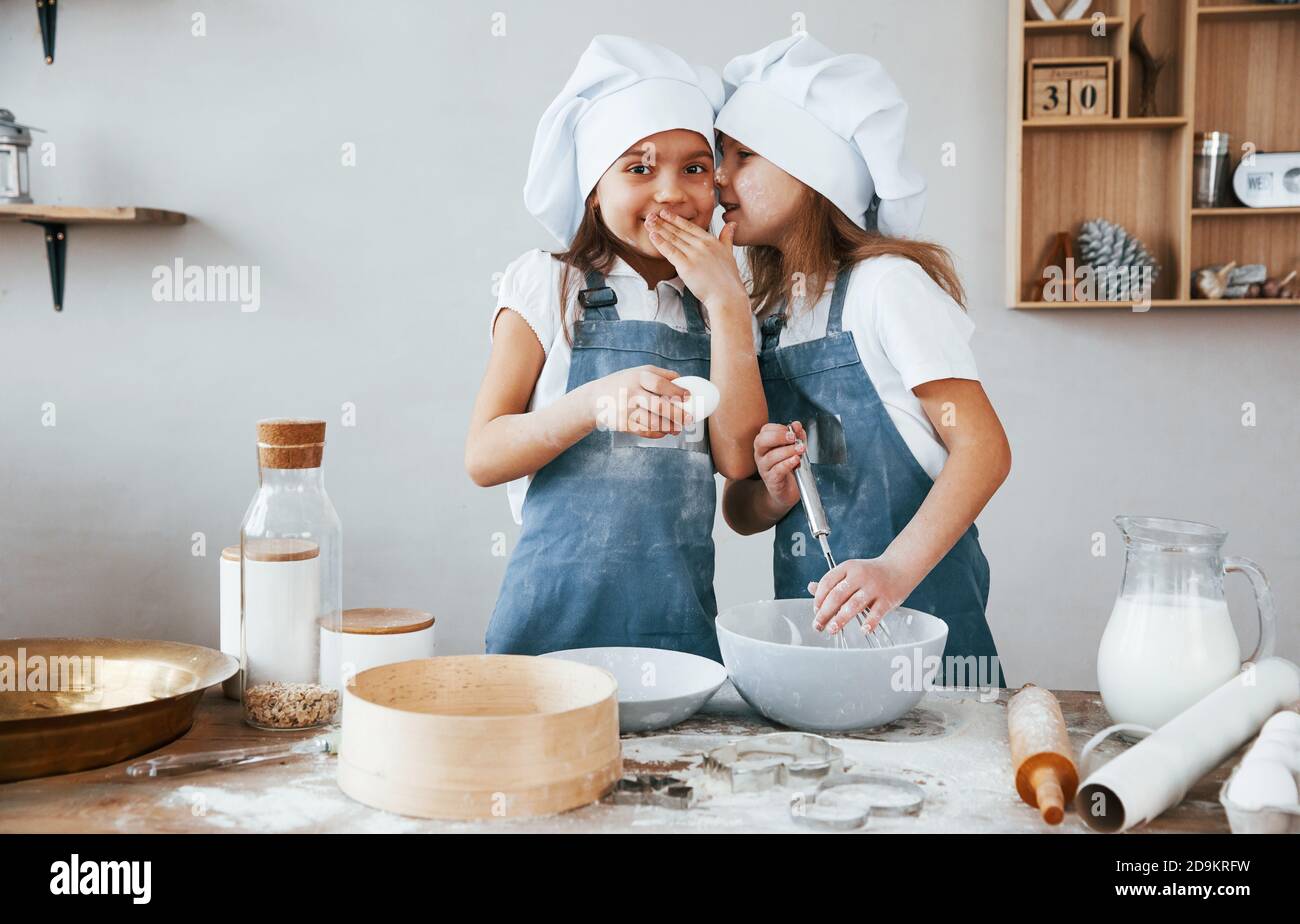 Two little girls in blue chef uniform talking secrets to each other ...