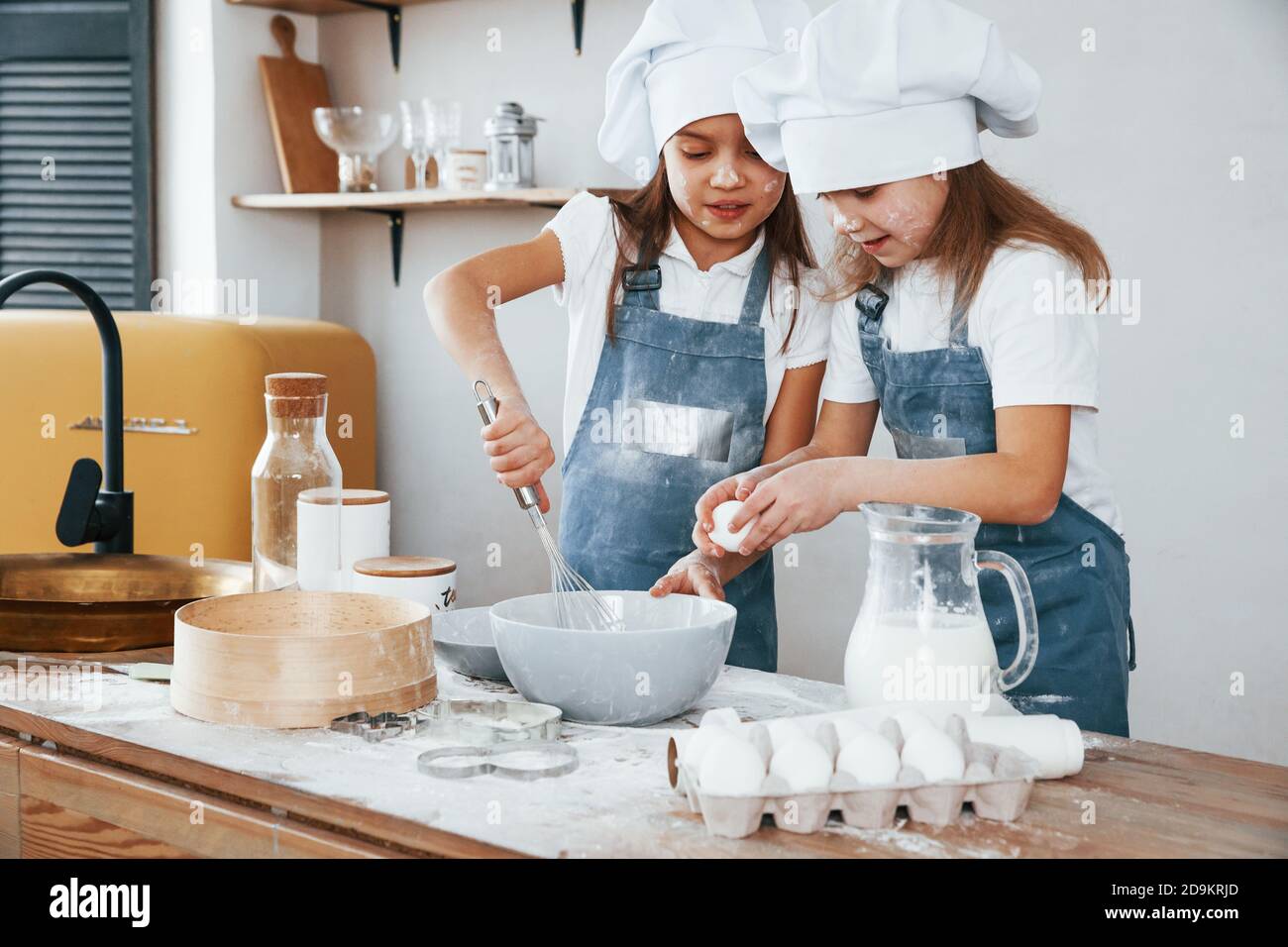 Two little girls in blue chef uniform mixing food on the kitchen by ...
