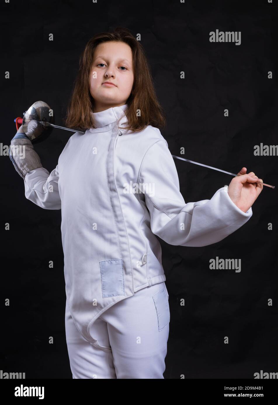 Teenage girl fencer dressed in uniform with epee and helmet studio ...