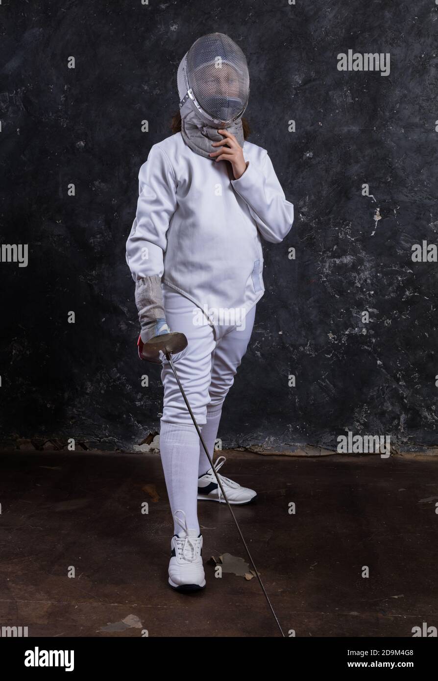 Teenage girl fencer dressed in uniform with epee and helmet studio ...