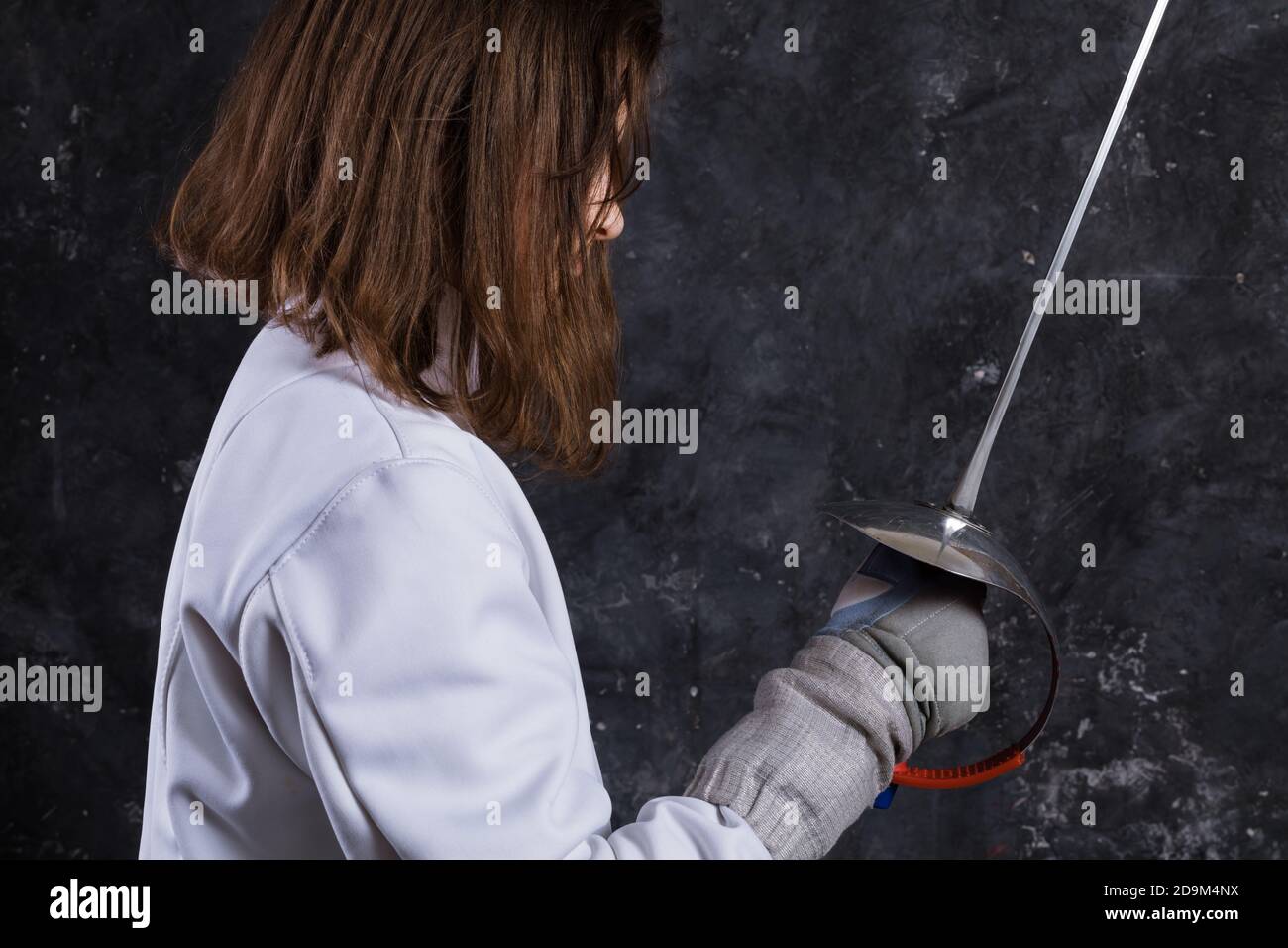 Teenage girl fencer dressed in uniform with epee and helmet studio ...