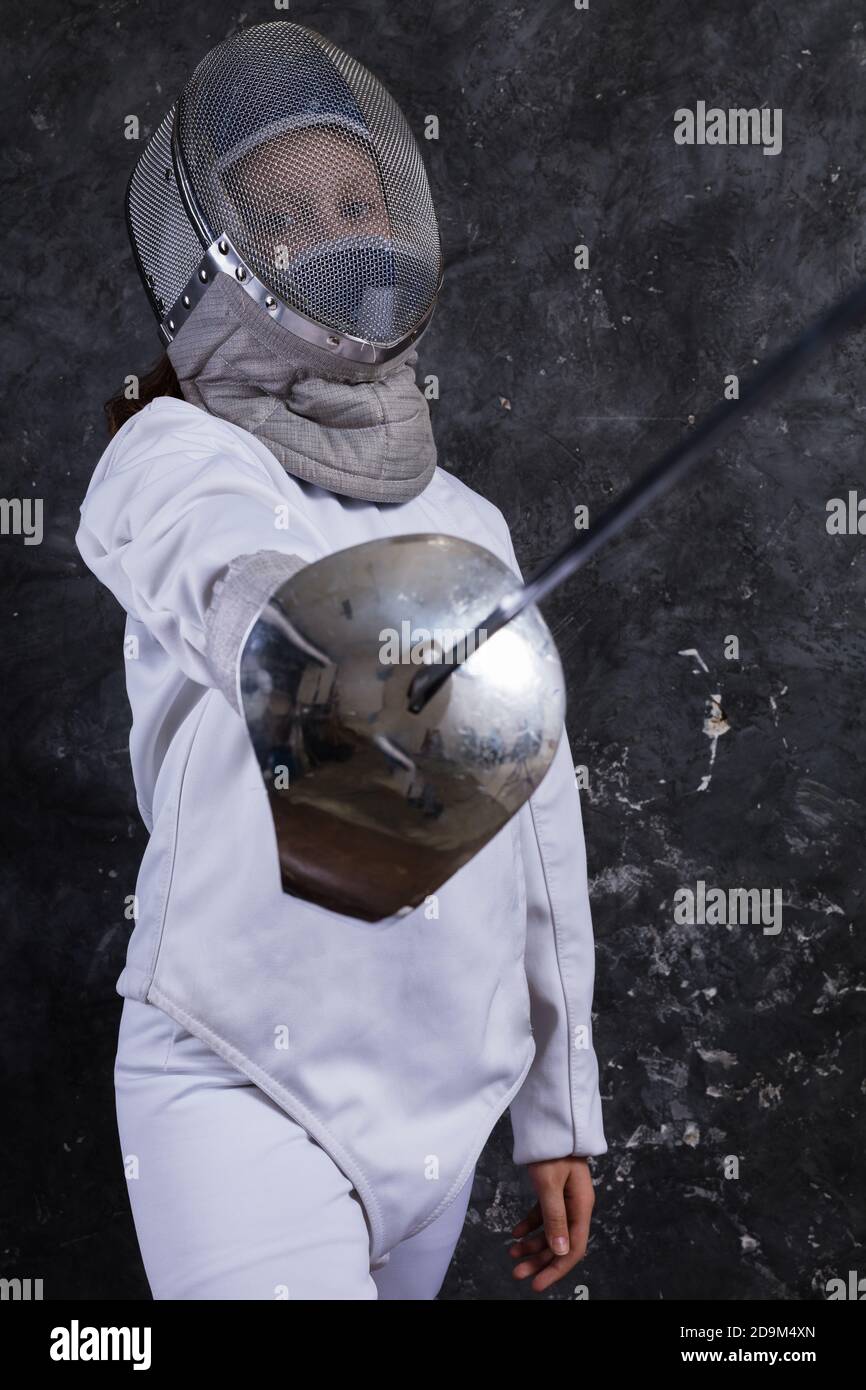 Teenage girl fencer dressed in uniform with epee and helmet studio ...