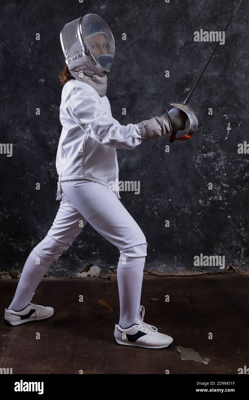 Teenage girl fencer dressed in uniform with epee and helmet studio ...