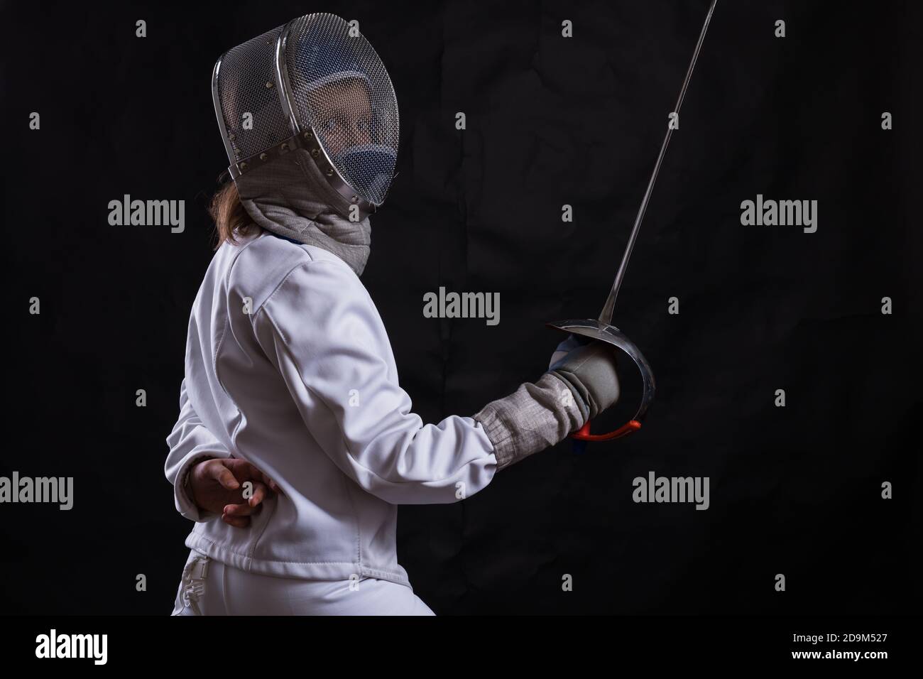 Teenage girl fencer dressed in uniform with epee and helmet studio ...