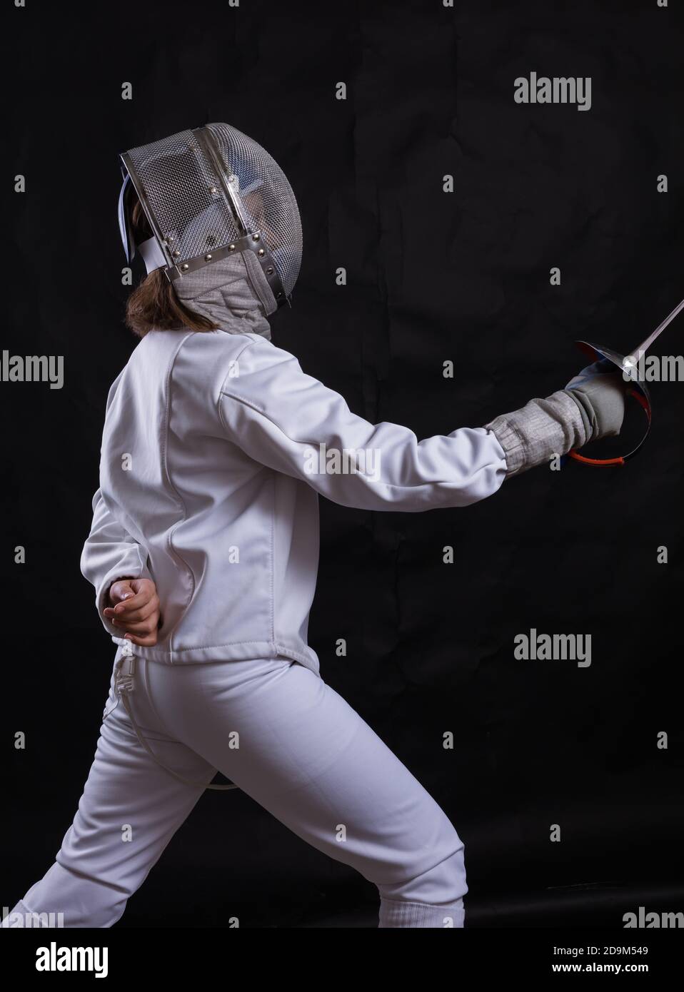 Teenage girl fencer dressed in uniform with epee and helmet studio ...