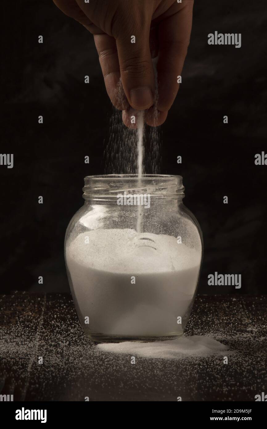Vertical shot of a person throwing a pinch of salt in a jar against a ...