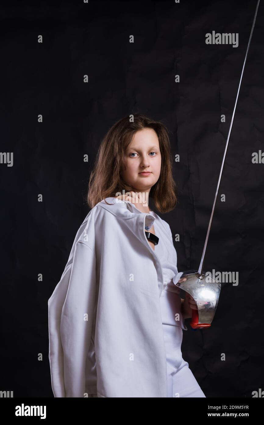 Teenage girl fencer dressed in uniform with epee and helmet studio ...