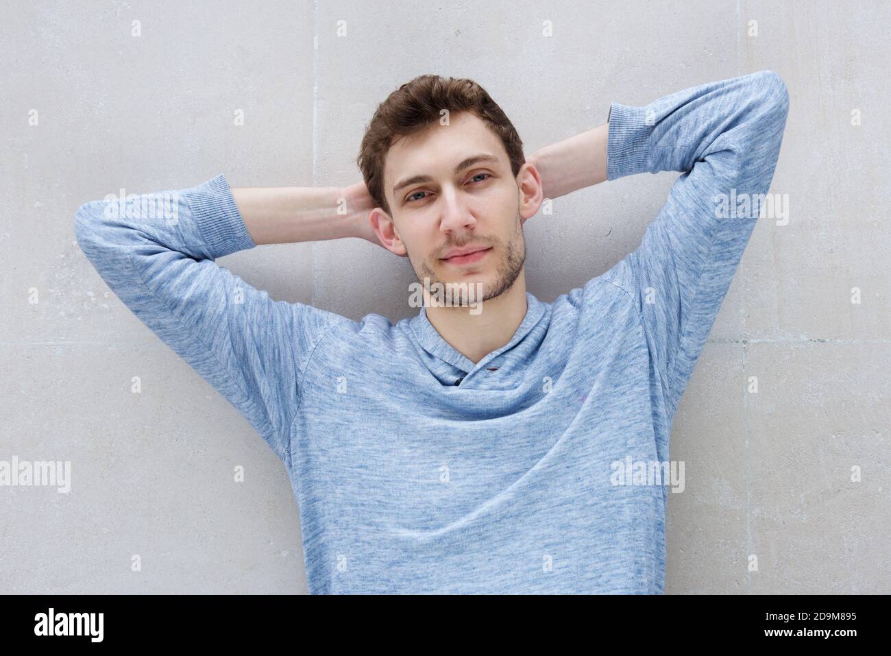 Close up portrait young man leaning against wall with hands behind head ...