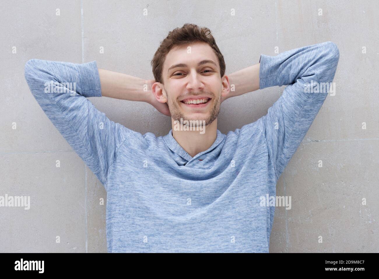 Close up portrait smiling young man leaning against wall with hands ...