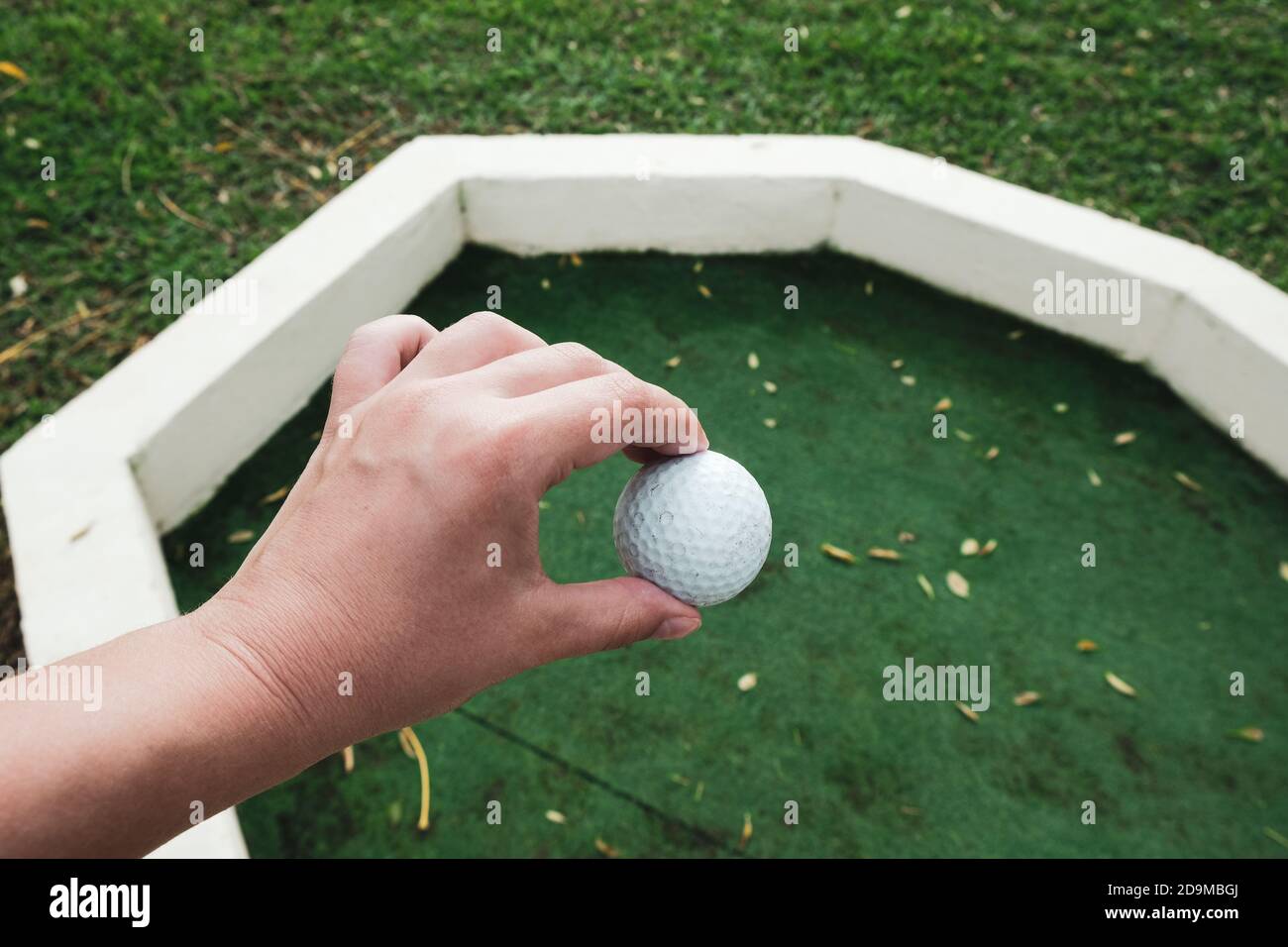White hand holding golf ball in its hole at field. Playing mini golf on ...