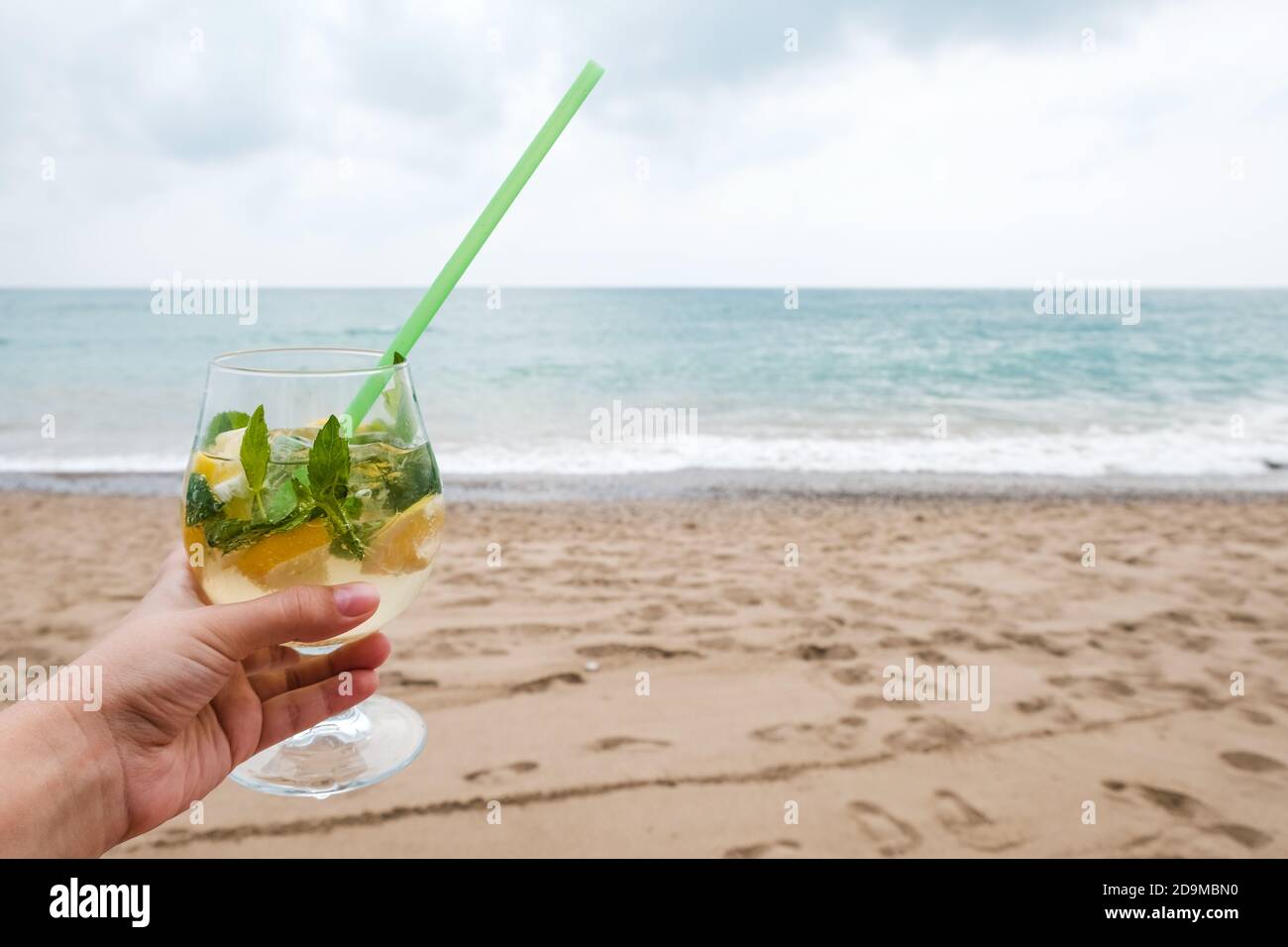 Luxury drink on sunny beach near the sea. Waves and sand in background. White female hand ...