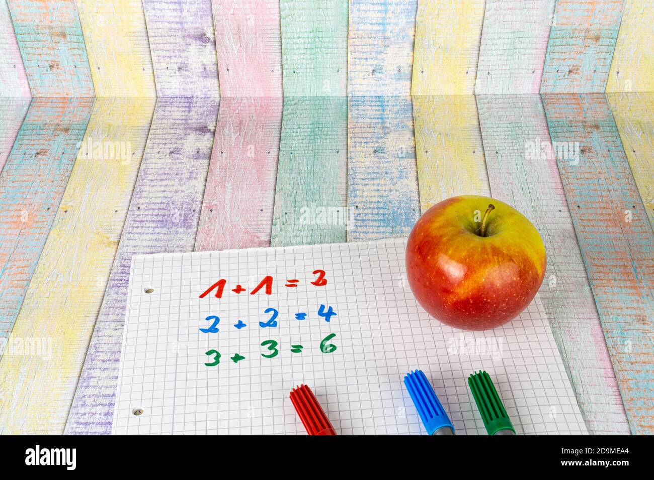 Block with simple calculating tasks and an apple on a colorful wooden ...