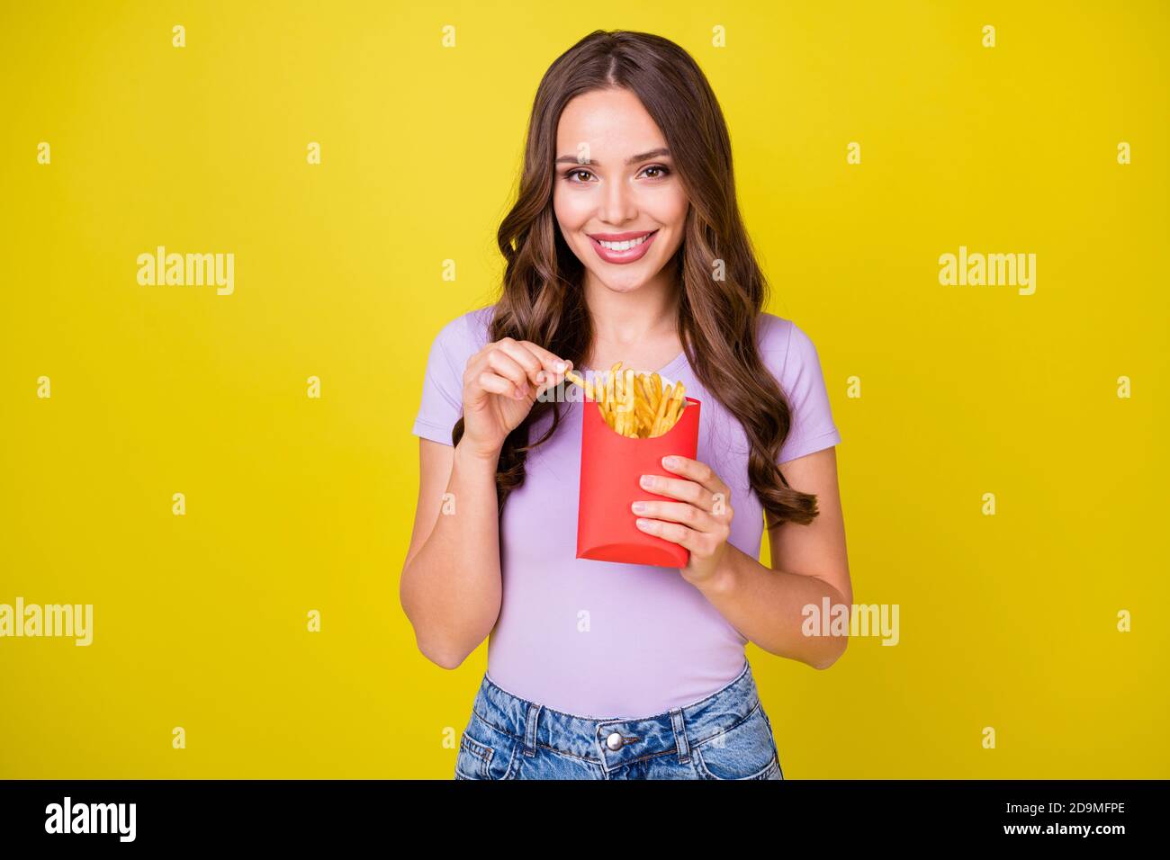Portrait of charming slim cheerful wavy-haired girl eating french fries ...
