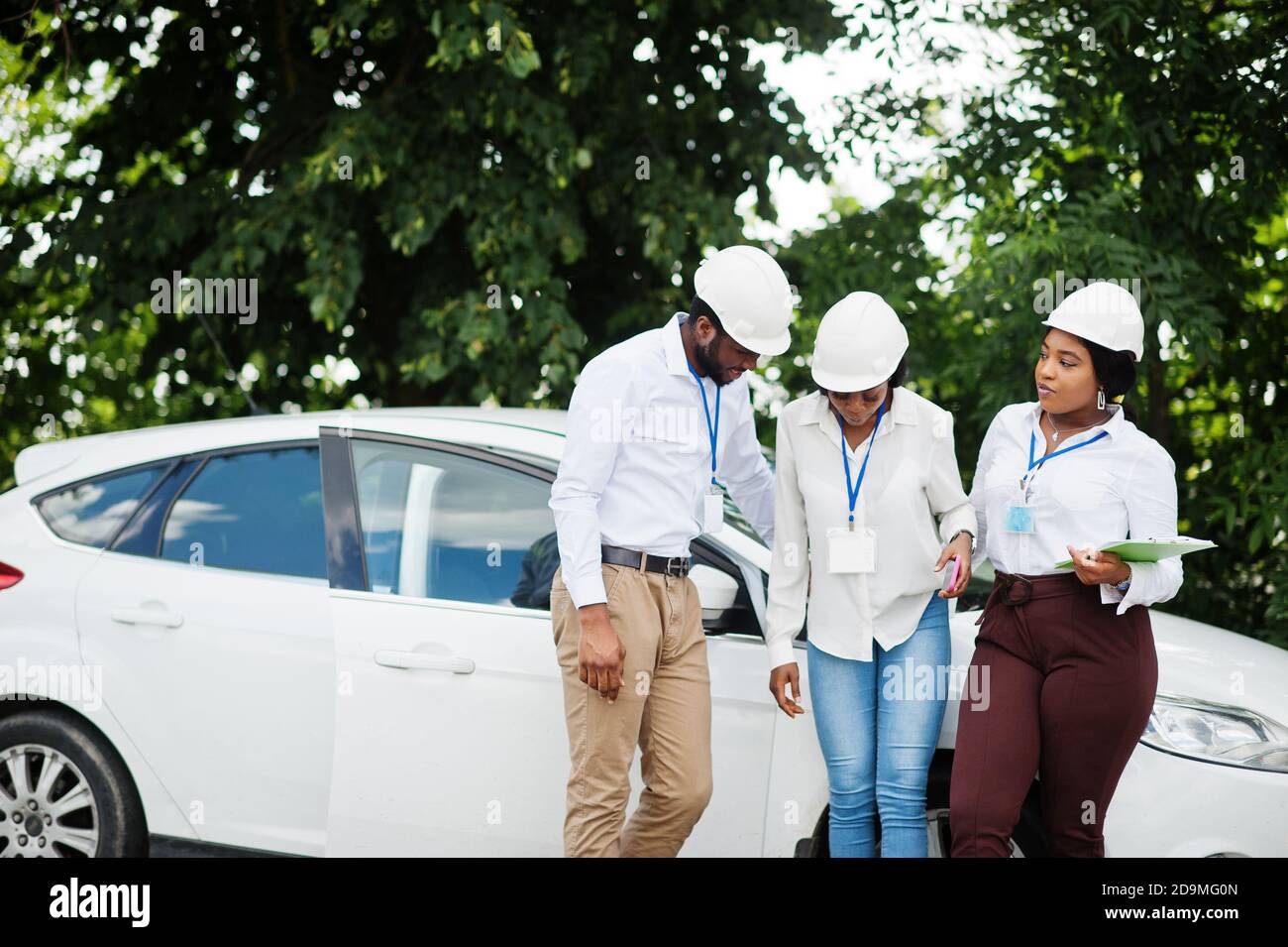 African american technician in white helmets near car. Group of three ...