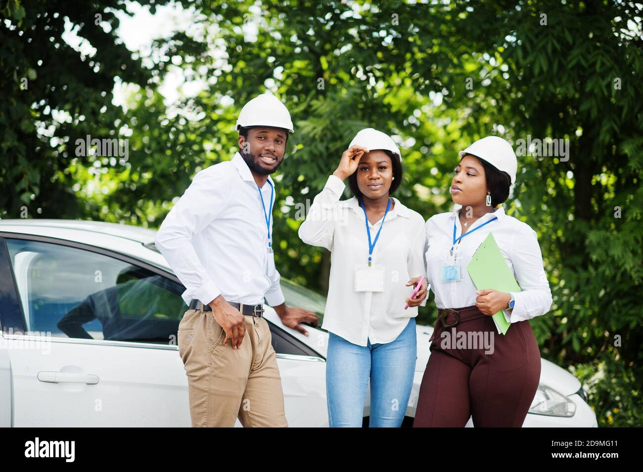 African american technician in white helmets near car. Group of three ...