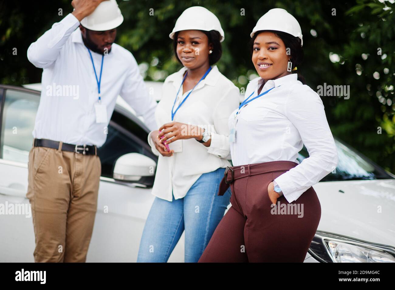 African american technician in white helmets near car. Group of three ...